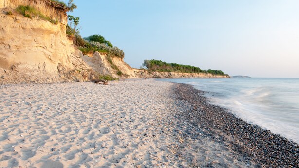 Uma praia com areal arenoso e uma área rochosa com vegetação.