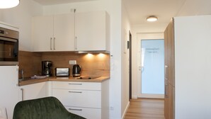 Cozinha moderna com armários brancos, bancada de madeira e área de refeições com uma cadeira verde e mesa posta para dois.