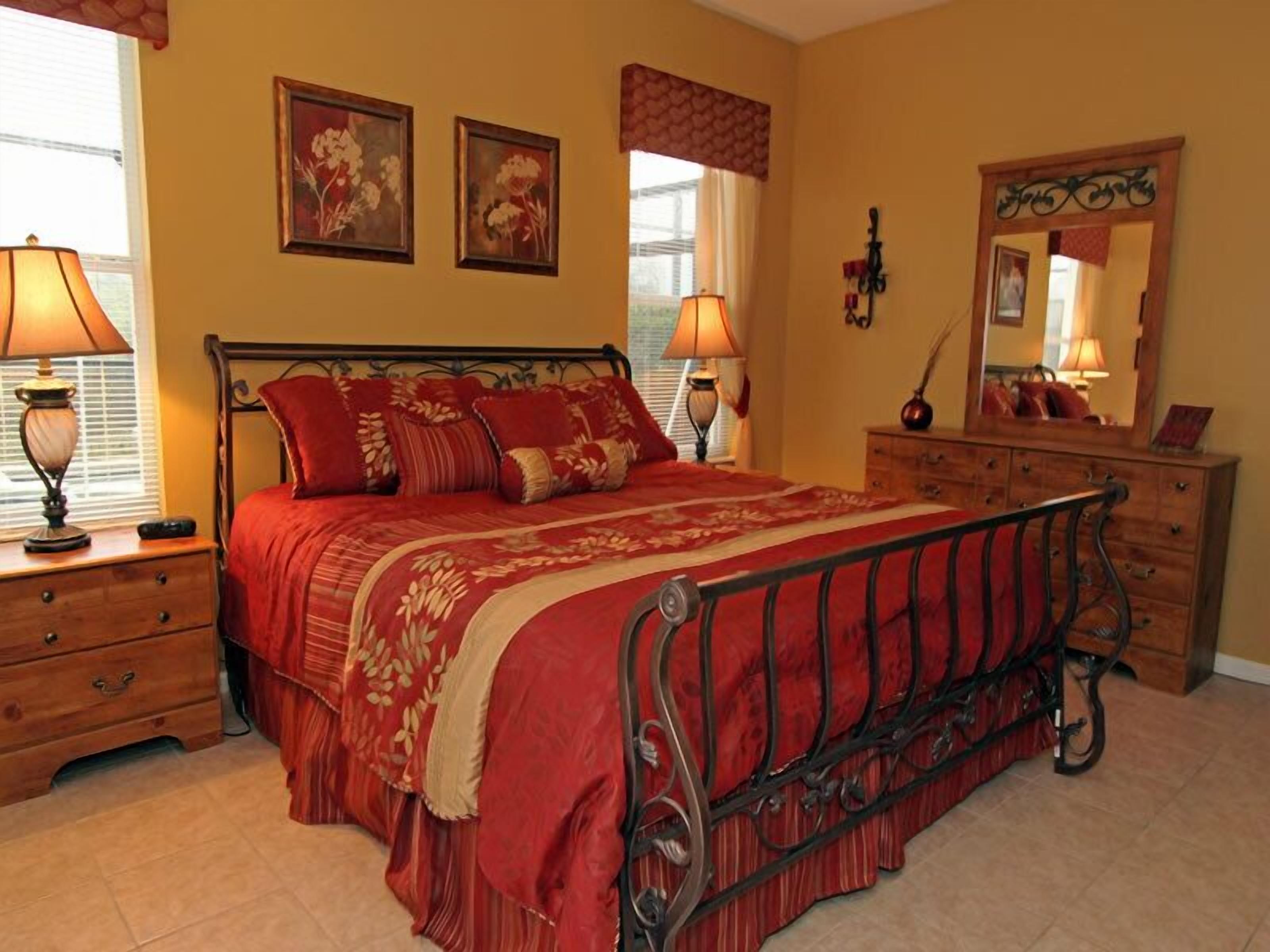 Quarto com estrutura de cama de metal, cômoda de madeira, duas mesas de cabeceira com abajures e um espelho grande acima da cômoda.