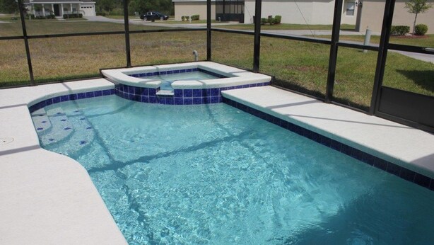 Piscina com hidromassagem, cercada por uma grade e gramado.