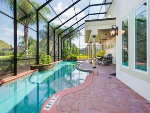 Piscina interior com teto de vidro, cercada por plantas e área de terraço com mobiliário para áreas externas.