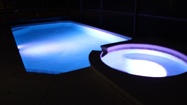 Piscina com borda iluminada em azul e área circular para hidromassagem.