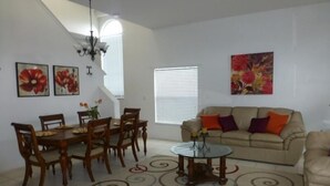 Uma área de refeições com mesa e cadeiras de madeira, um sofá com almofadas coloridas e um tapete decorativo com desenhos espirais.