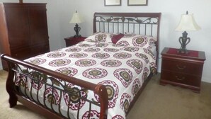 Quarto com cama, duas mesas de cabeceira, um criado-mudo e cômoda, com duas imagens emolduradas na parede.