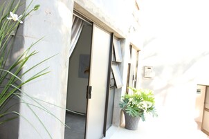 Uma porta que dá para um quarto com uma planta em vaso e uma janela com cortinas.