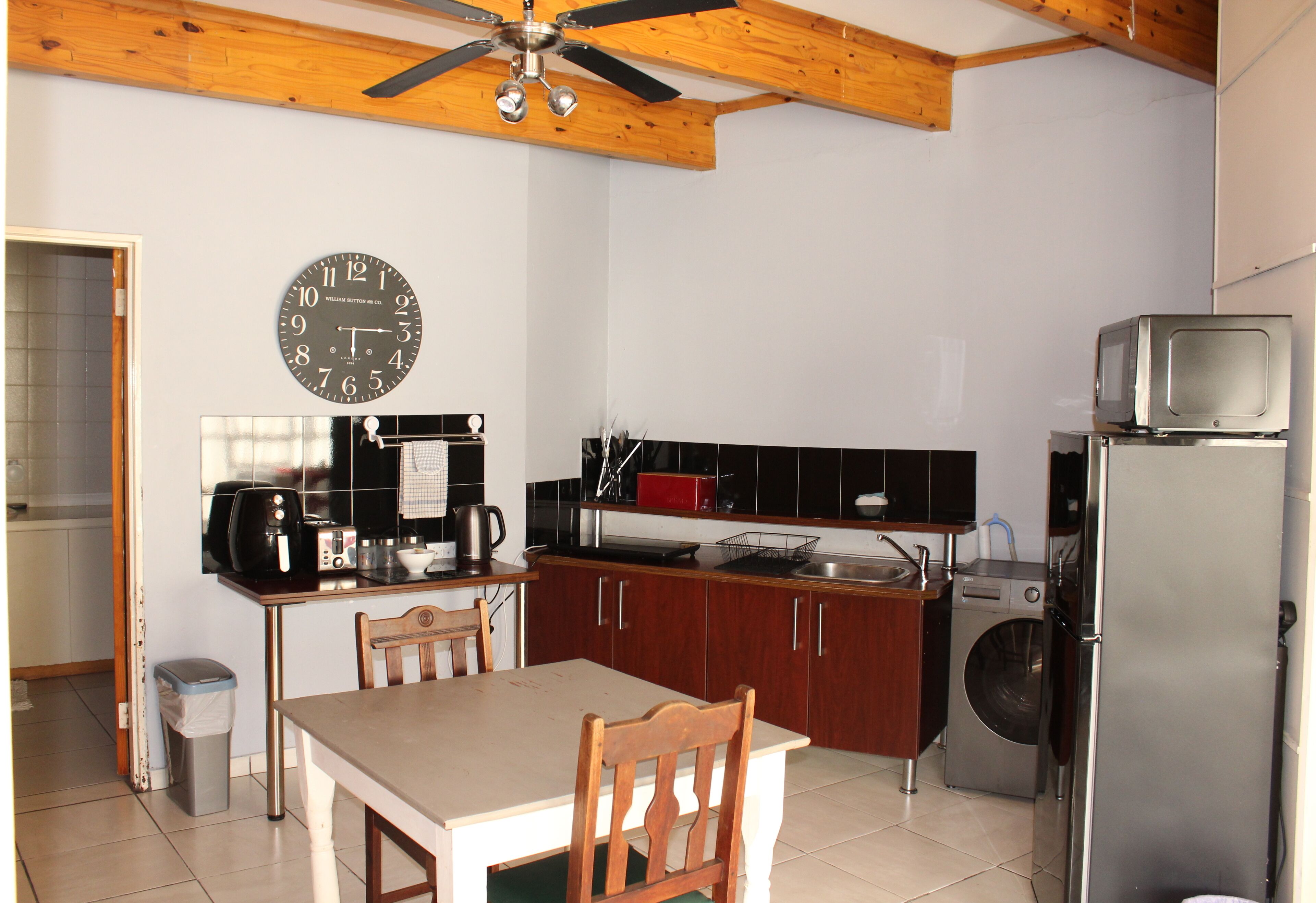 Uma cozinha compacta com armários de madeira, uma mesa de jantar, um ventilador de teto, micro-ondas e máquina de lavar.