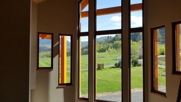 Quarto com grandes janelas que oferecem vista para uma paisagem verde com árvores e um pequeno edifício.