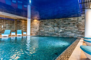 Uma piscina interior com água cristalina, paredes de pedra e espreguiçadeiras.