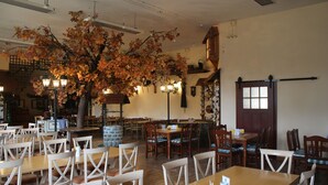 Um restaurante com mesas e cadeiras de madeira, uma grande árvore com folhas de outono e lanternas penduradas.