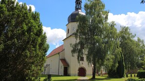 Uma igreja com uma cúpula imponente e um campanário, rodeada por vegetação exuberante.