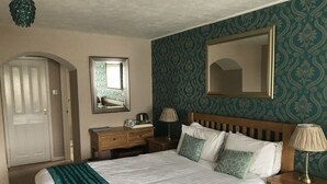 Quarto bem arrumado com cama, mesas de cabeceira, cômoda, espelho e porta.