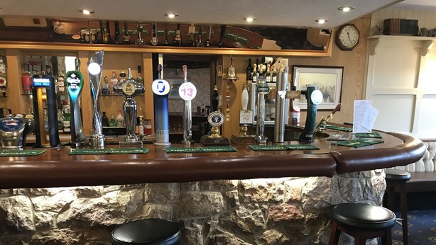 Uma área de bar com várias torneiras de cerveja, banquetas e um fundo de parede de pedra.