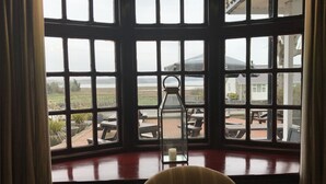 Quarto com uma grande janela saliente com vista para uma área gramada com mesas de piquenique e um edifício ao longe.