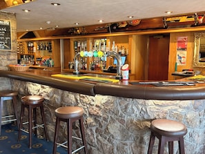 Uma área de bar com parede de pedra, banquetas, balcão e variedade de garrafas e copos.