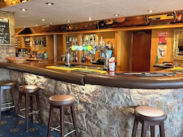 Uma área de bar com parede de pedra, banquetas, balcão e variedade de garrafas e copos.