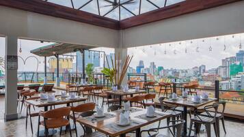 Um restaurante no terraço com mesas preparadas para refeições, vista da cidade e estrutura de teto de madeira.