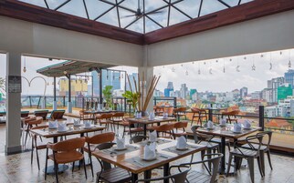 Um restaurante no terraço com mesas preparadas para refeições, vista da cidade e estrutura de teto de madeira.