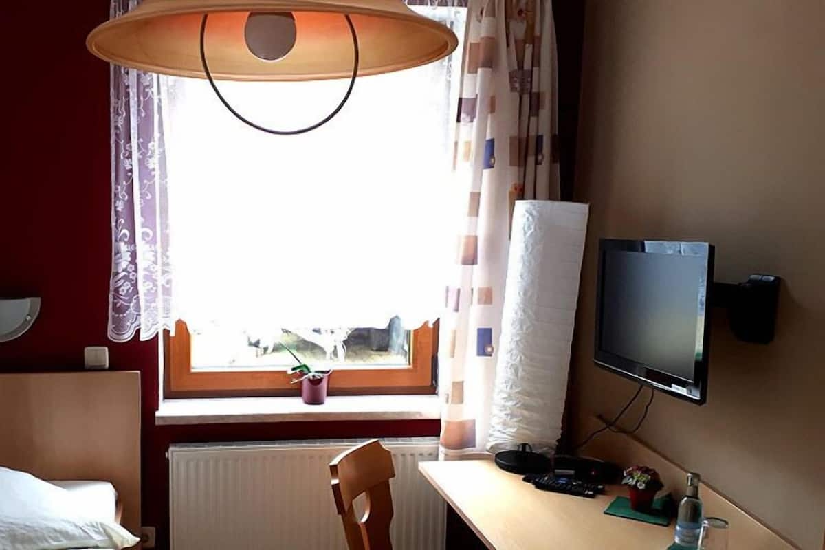 Quarto de hotel com cama, escrivaninha com computador, televisão e janela com cortinas.