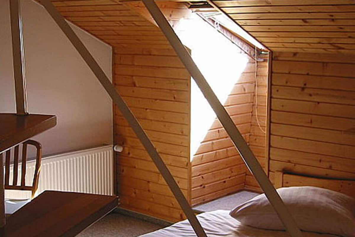Um pequeno quarto de cabana de madeira, com uma cama beliche, uma cadeira e uma janela que oferece luz natural.
