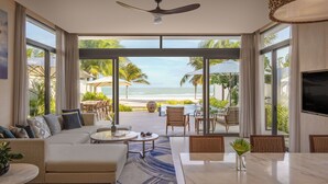 Sala moderna com um sofá grande, uma mesa de jantar e cadeiras, com vista para uma praia com palmeiras e do oceano.