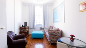 Um espaço compacto com sofá, uma cadeira, uma mesa pequena e uma televisão sobre um móvel de madeira.