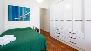 Quarto com colcha verde, guarda-roupa branco e um quadro abstrato azul na parede.
