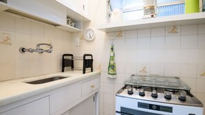 Cozinha com bancada branca, pia, fogão e relógio na parede.