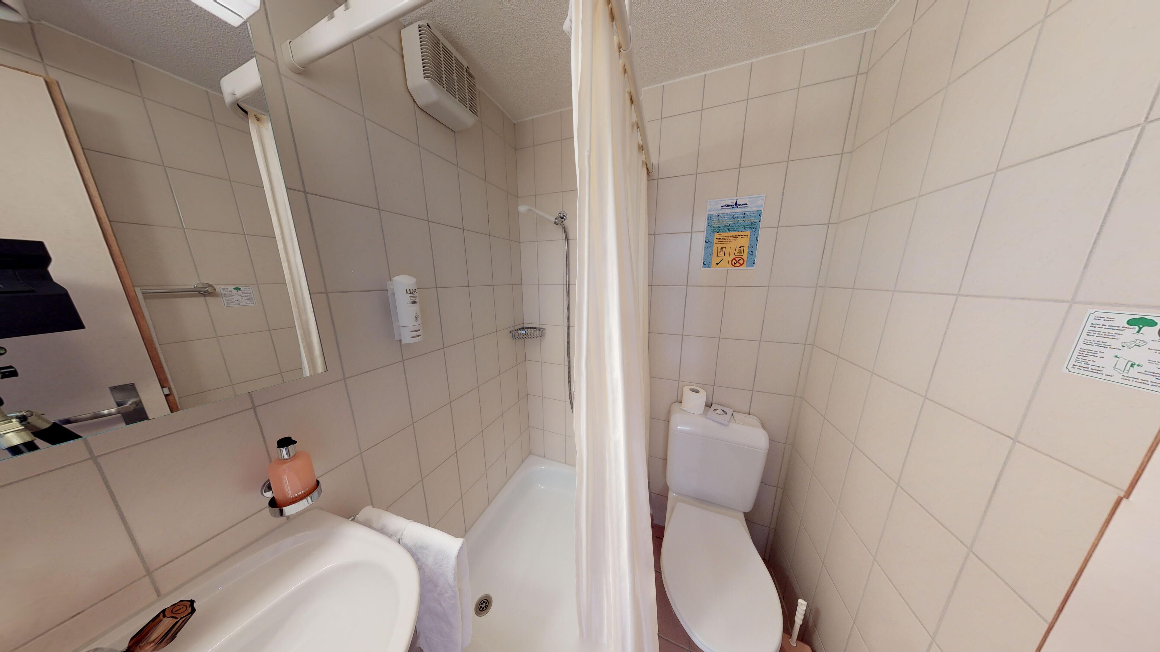 Um banheiro pequeno, com revestimento de azulejos, chuveiro, vaso sanitário e pia.