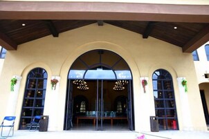 Entrada de um edifício com varanda coberta, grandes janelas em arco e luminárias penduradas.