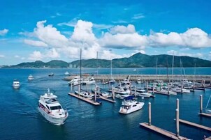 Uma marina com vários barcos atracados em cais, cercada por água e montanhas ao longe.