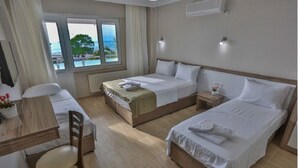 Quarto de hotel com duas camas, uma escrivaninha e uma cadeira. Há uma janela com vista para o mar e uma árvore.