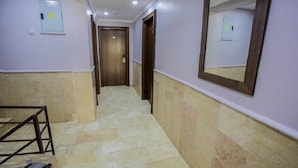 Um corredor com chão de azulejos, uma porta de madeira no final e um espelho na parede.