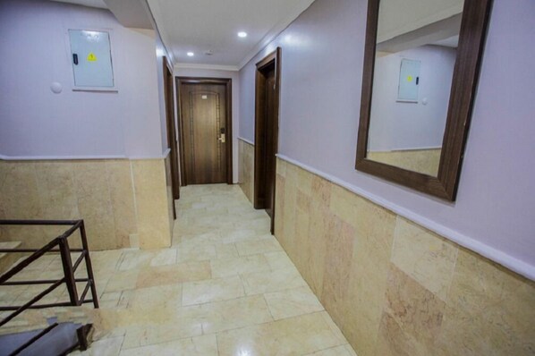 Um corredor com chão de azulejos, uma porta de madeira no final e um espelho na parede.