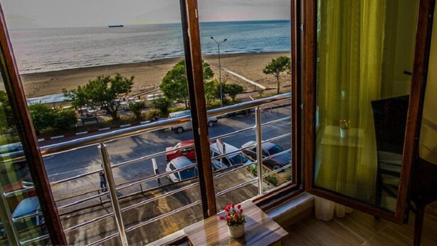 Quarto com uma janela ampla de frente para a praia e um estacionamento.