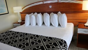 Quarto de hotel com uma cama grande, cabeceira de madeira com decoração em estrela, roupa de cama branca e um cobertor estampado em preto e branco.