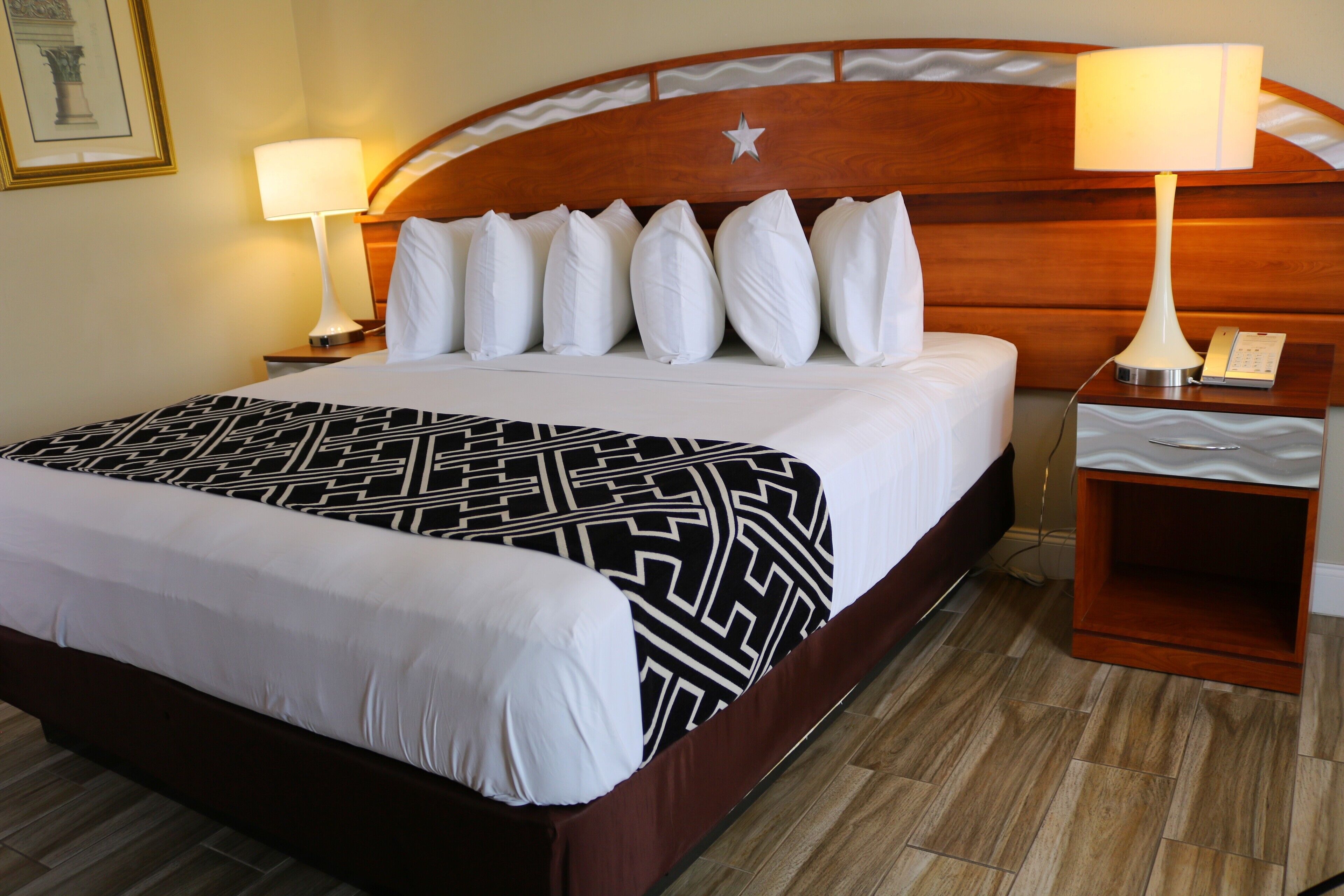 Uma cama bem arrumada com colcha estampada, cabeceira de madeira com desenho de estrela, duas luminárias de cabeceira e uma mesa de cabeceira com telefone.