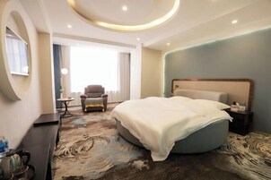 Quarto de hotel com uma cama grande, uma escrivaninha, uma cadeira e uma mesinha.