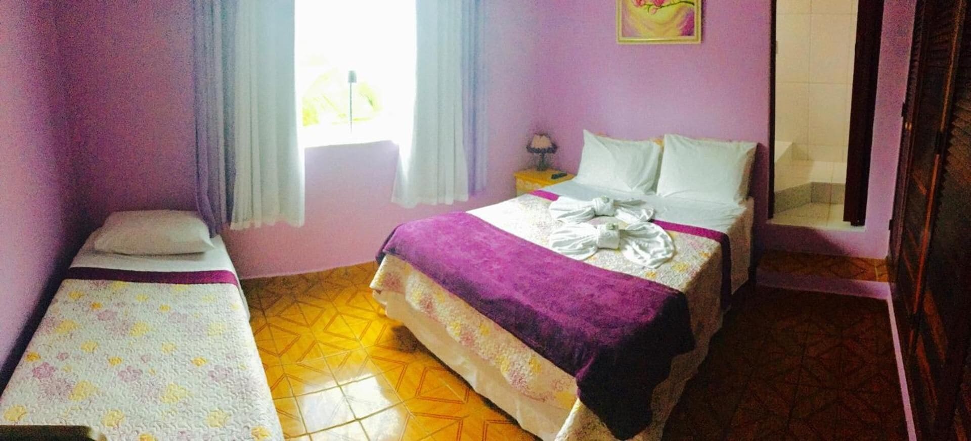 Quarto com cama, mesa de cabeceira e janela com cortinas.