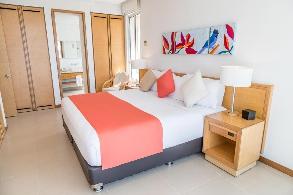 Quarto de hotel com cama, mesa de cabeceira, luminária e um quadro na parede.