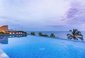 Uma piscina infinita com vista para o oceano e palmeiras.