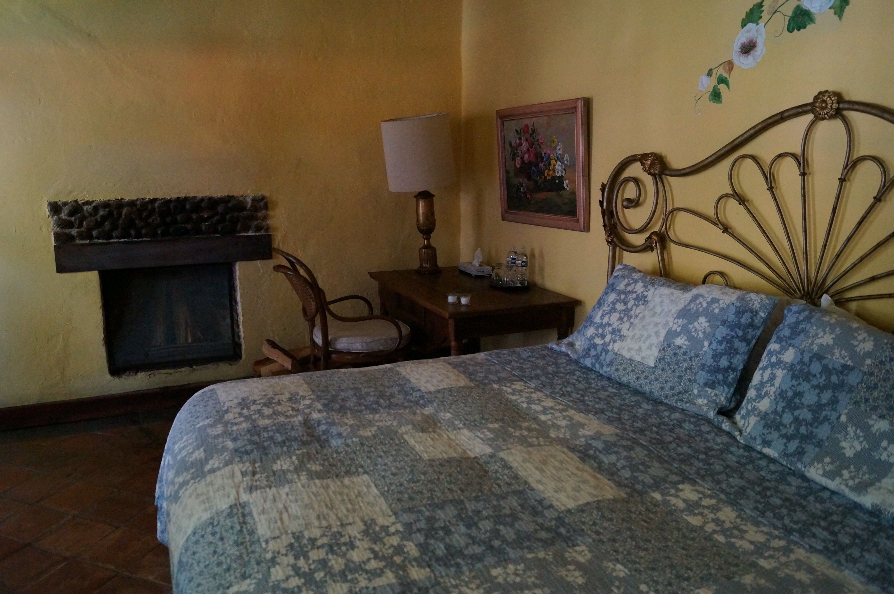 Um quarto com cama, mesa de cabeceira, cadeira, luminária e um quadro na parede.