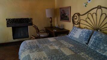 Um quarto com cama, mesa de cabeceira, cadeira, luminária e um quadro na parede.