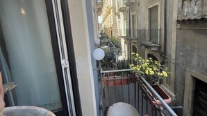 Uma rua estreita na cidade, com edifícios de ambos os lados, uma varanda com plantas em vasos e uma porta para um quarto.