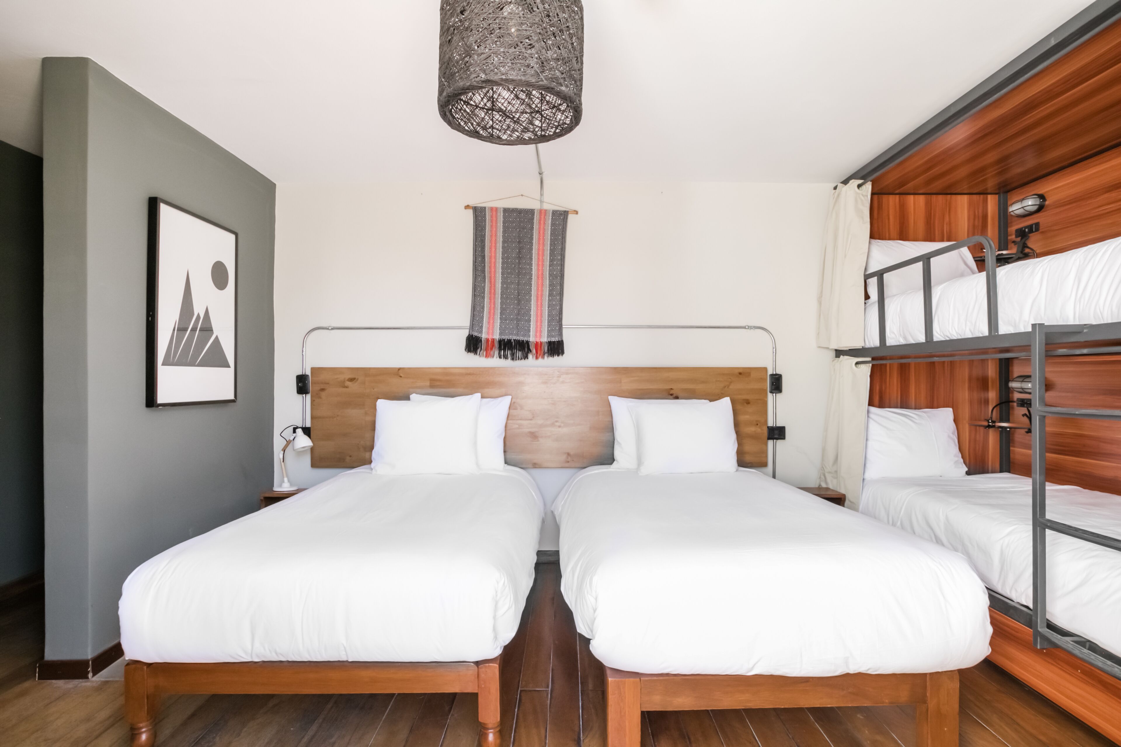 Quarto com duas camas de solteiro, uma cama beliche, um lustre pendurado e um quadro na parede.