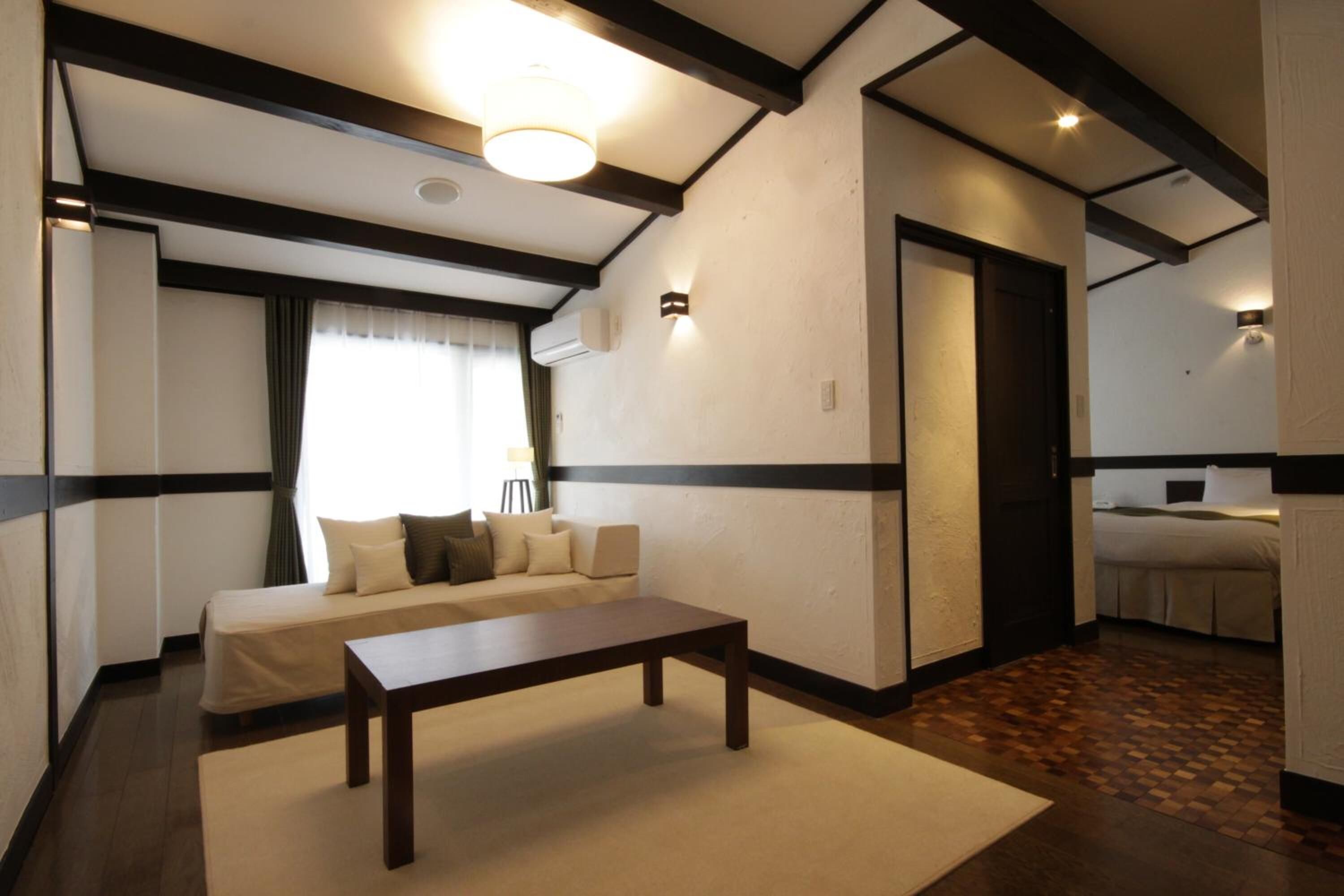 Quarto de hotel com cama, sofá, mesa e piso de madeira.