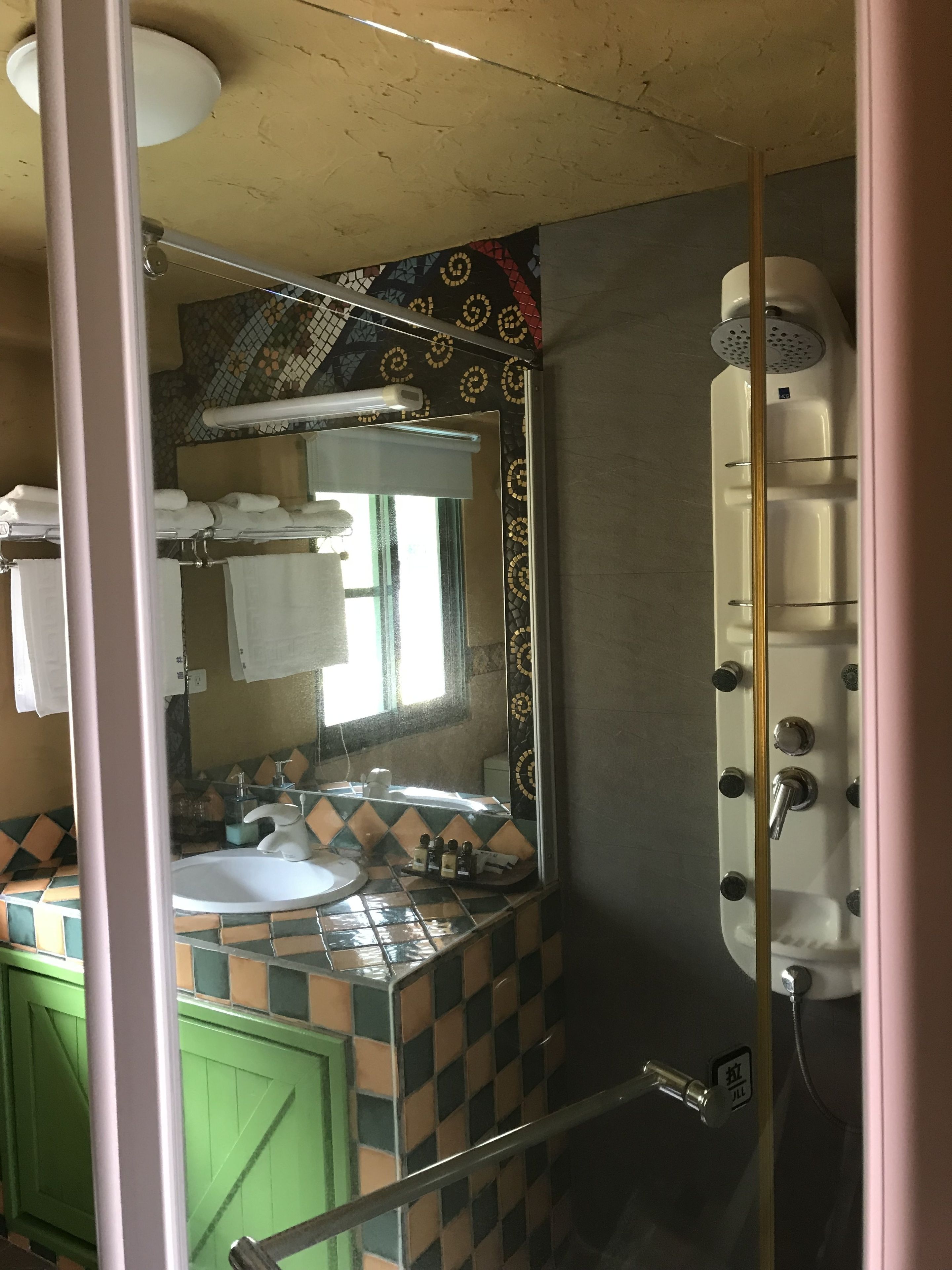 Uma casa de banho com chão em azulejo, lavatório, espelho, chuveiro e um armário verde.