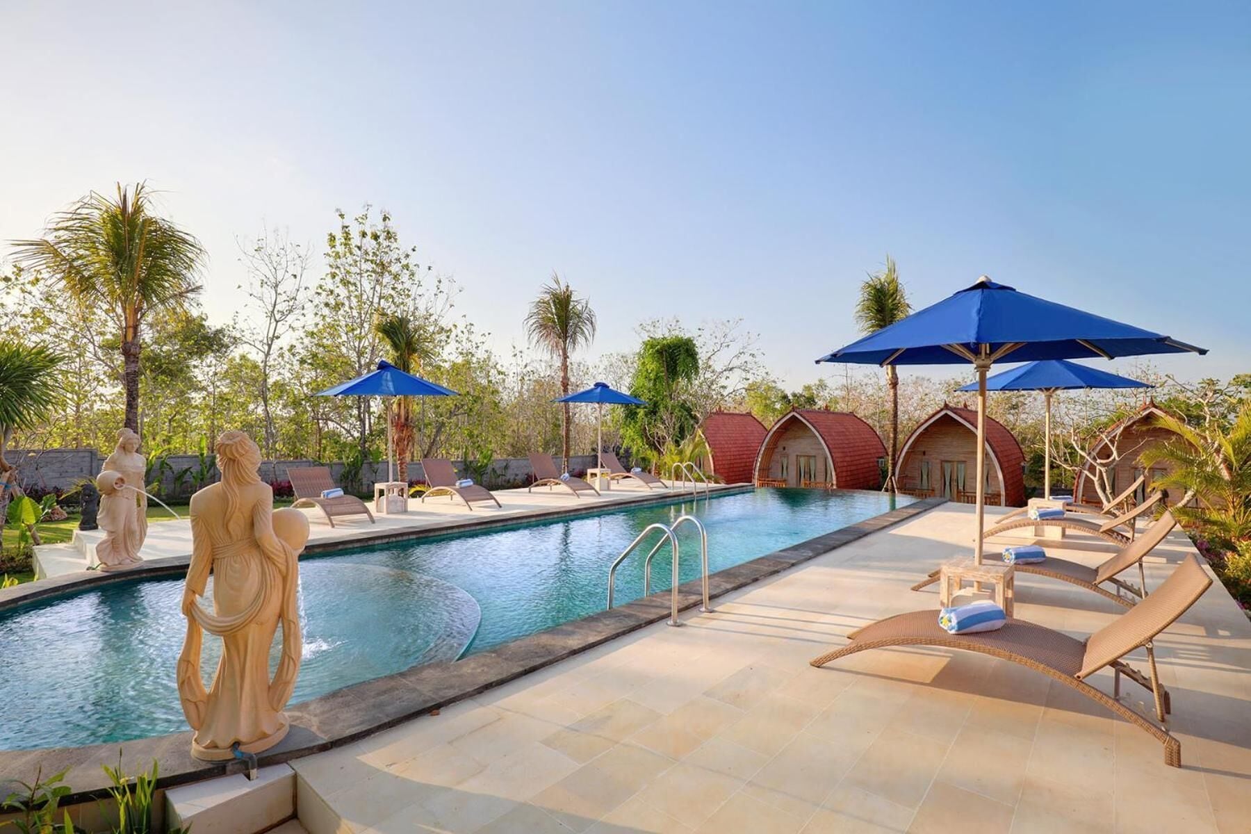Área de piscina com espreguiçadeiras, guarda-sóis e uma estátua.