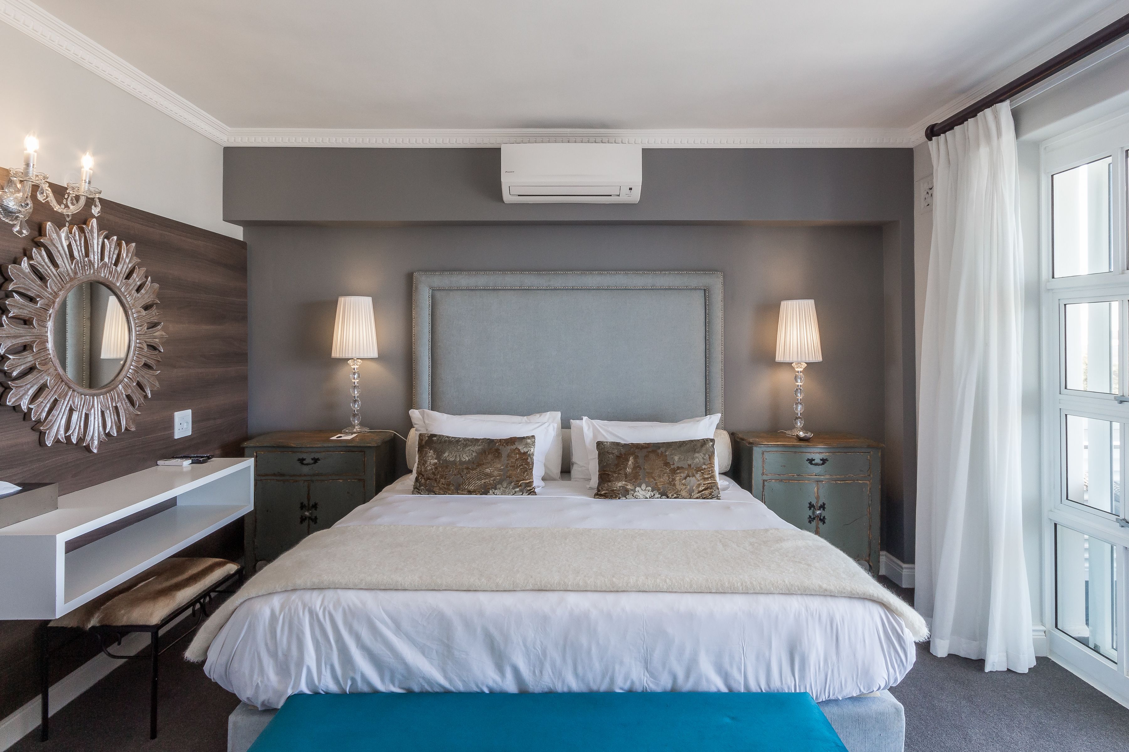 Quarto de hotel com uma cama grande, duas mesas de cabeceira com luminárias, uma penteadeira com espelho e uma janela com cortinas.