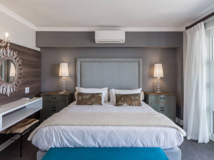 Quarto de hotel com uma cama grande, duas mesas de cabeceira com luminárias, uma penteadeira com espelho e uma janela com cortinas.