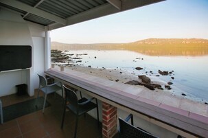 Terraço com vista para um lago tranquilo e colinas distantes, com uma mesa comprida e cadeiras.